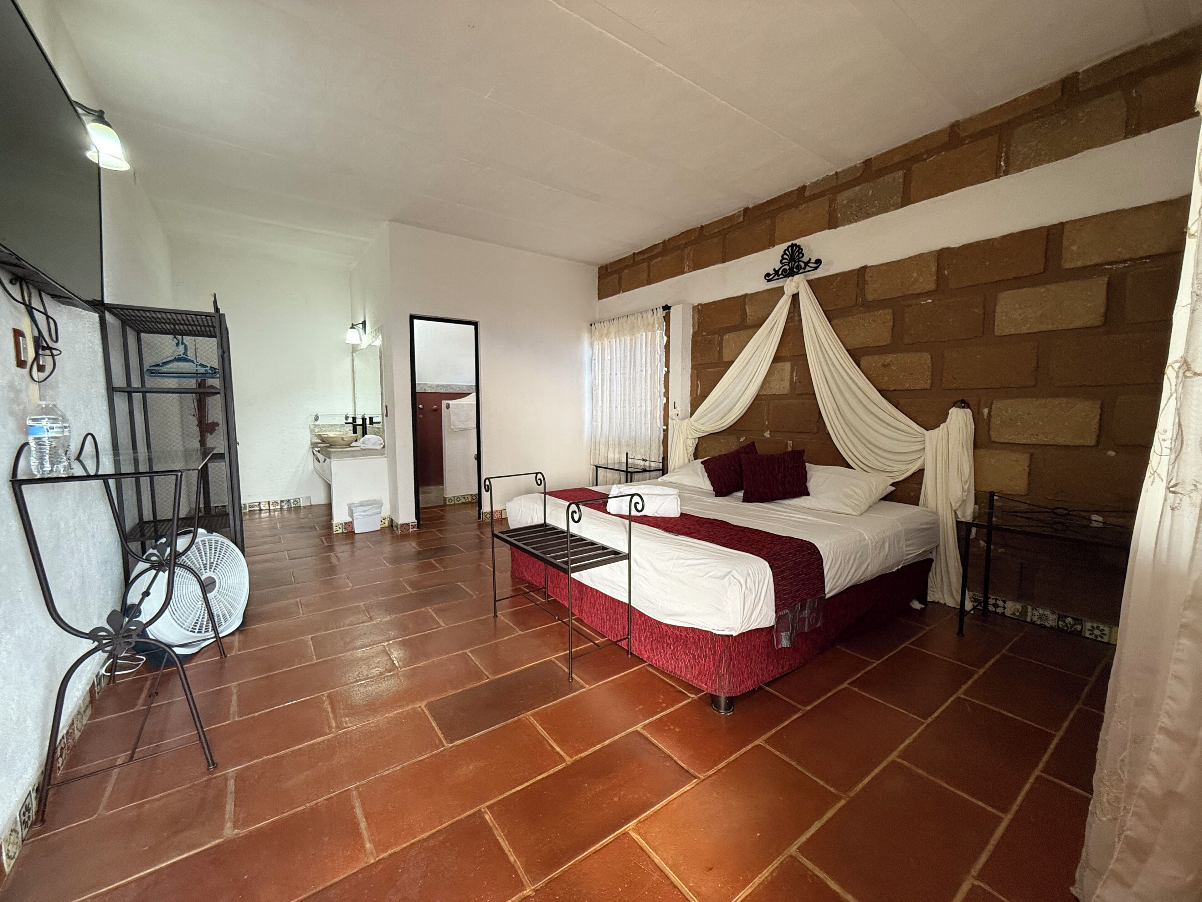 Um quarto com uma cama, mesa de cabeceira, espelho, ventoinha e guarda-roupa.