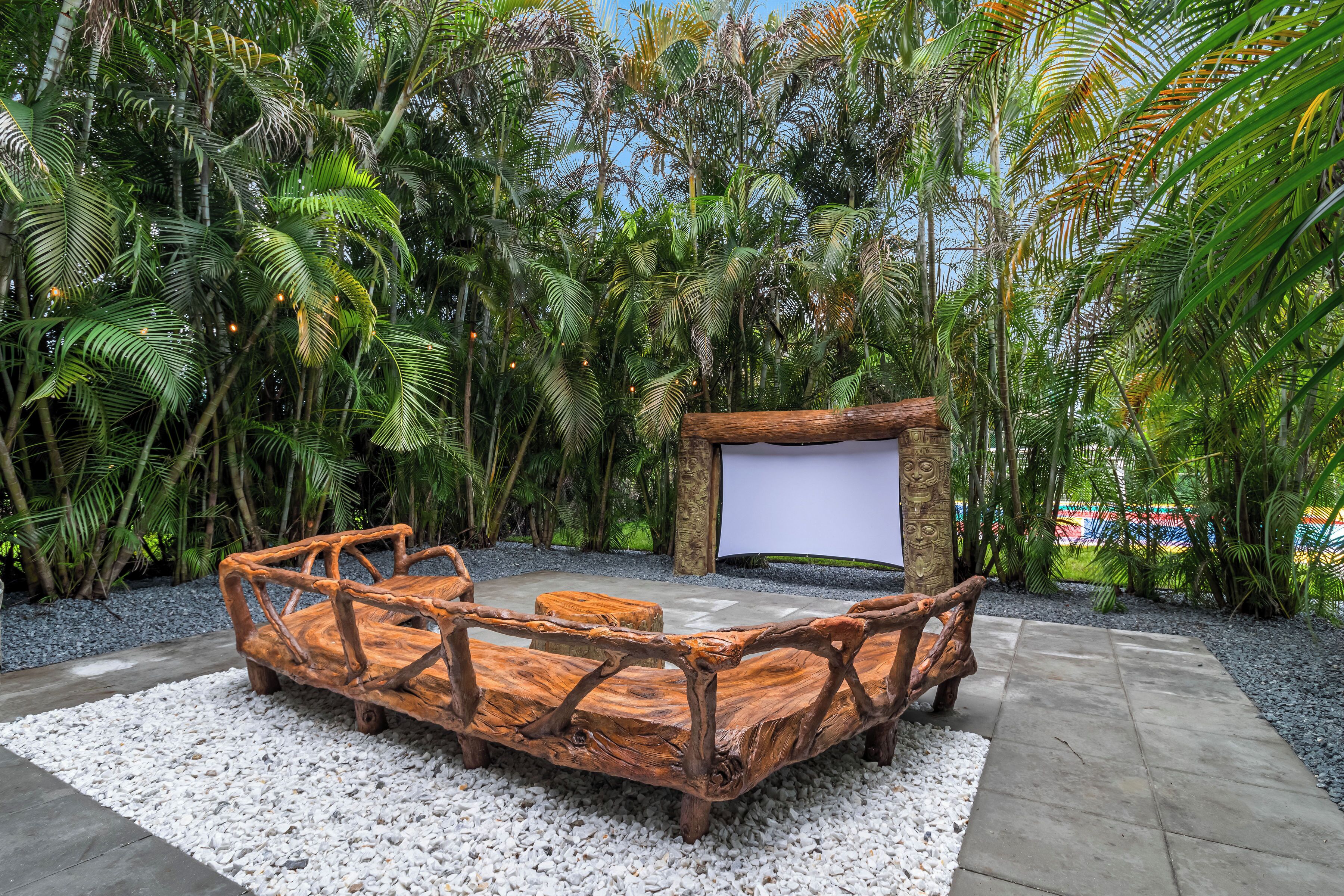 Um banco de madeira com design rústico, rodeado por um jardim com diversas plantas tropicais.