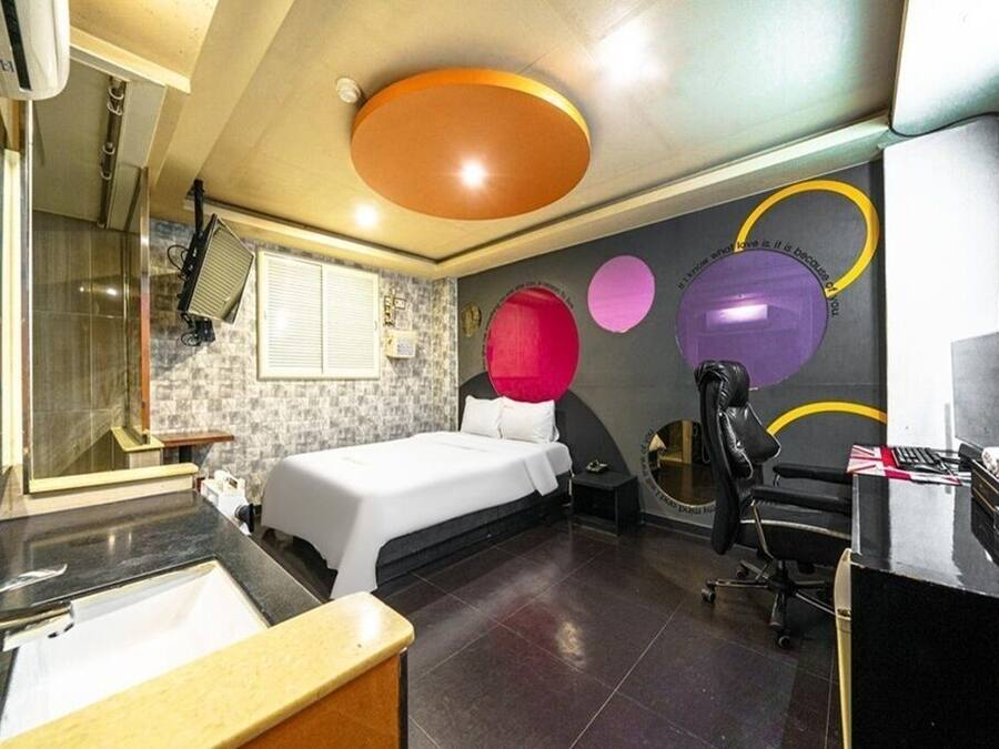 Quarto de hotel moderno com uma cama grande, uma escrivaninha, uma cadeira, banheiro com pia e chuveiro.