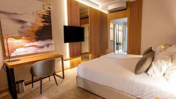 Quarto de hotel com cama, escrivaninha, cadeira, televisão e um quadro na parede.