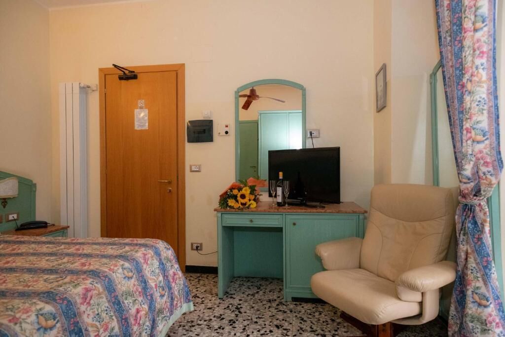 Quarto com cama, escrivaninha com computador, cadeira e espelho.