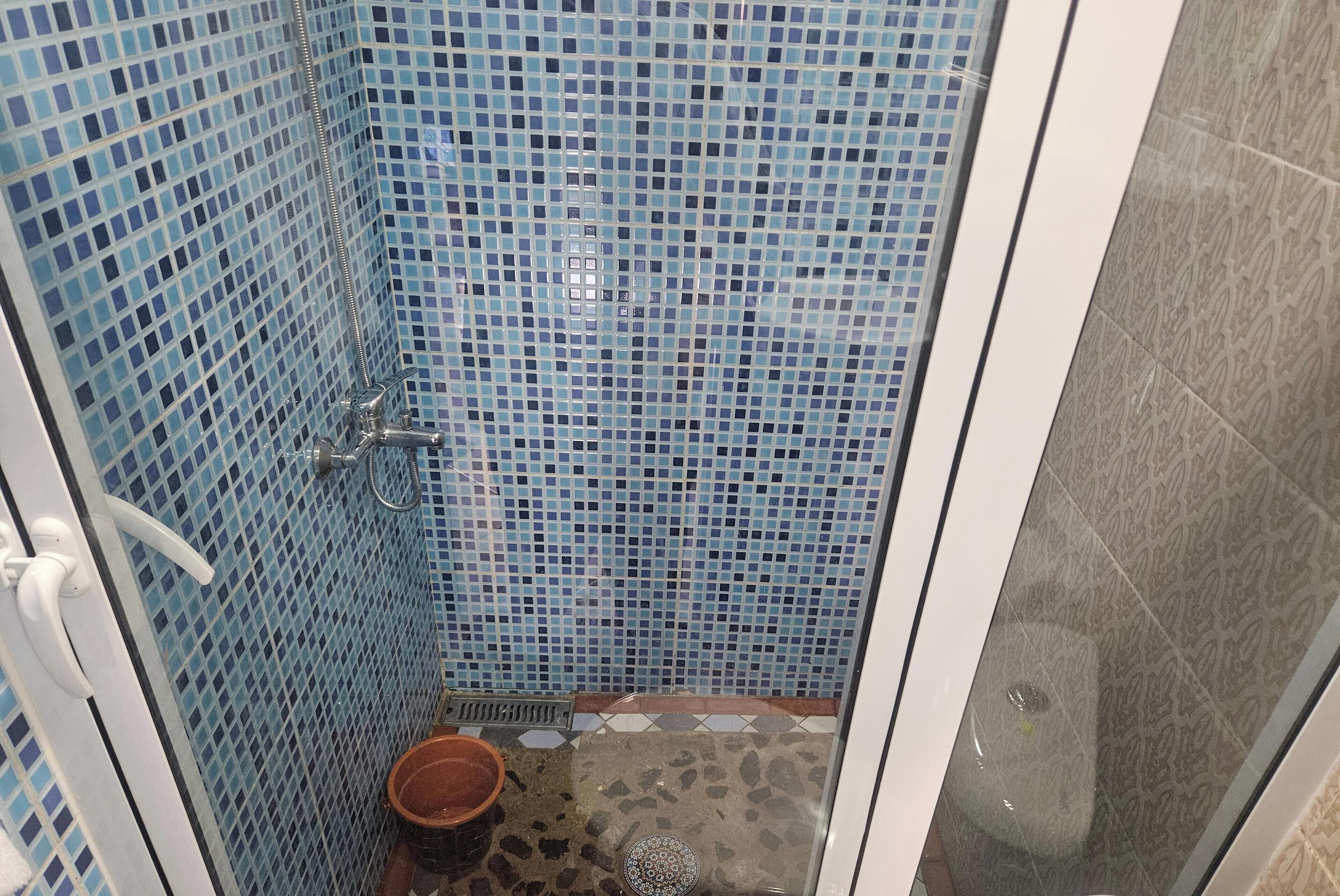Um chuveiro com azulejos de mosaico azul, um chuveiro e um ralo.