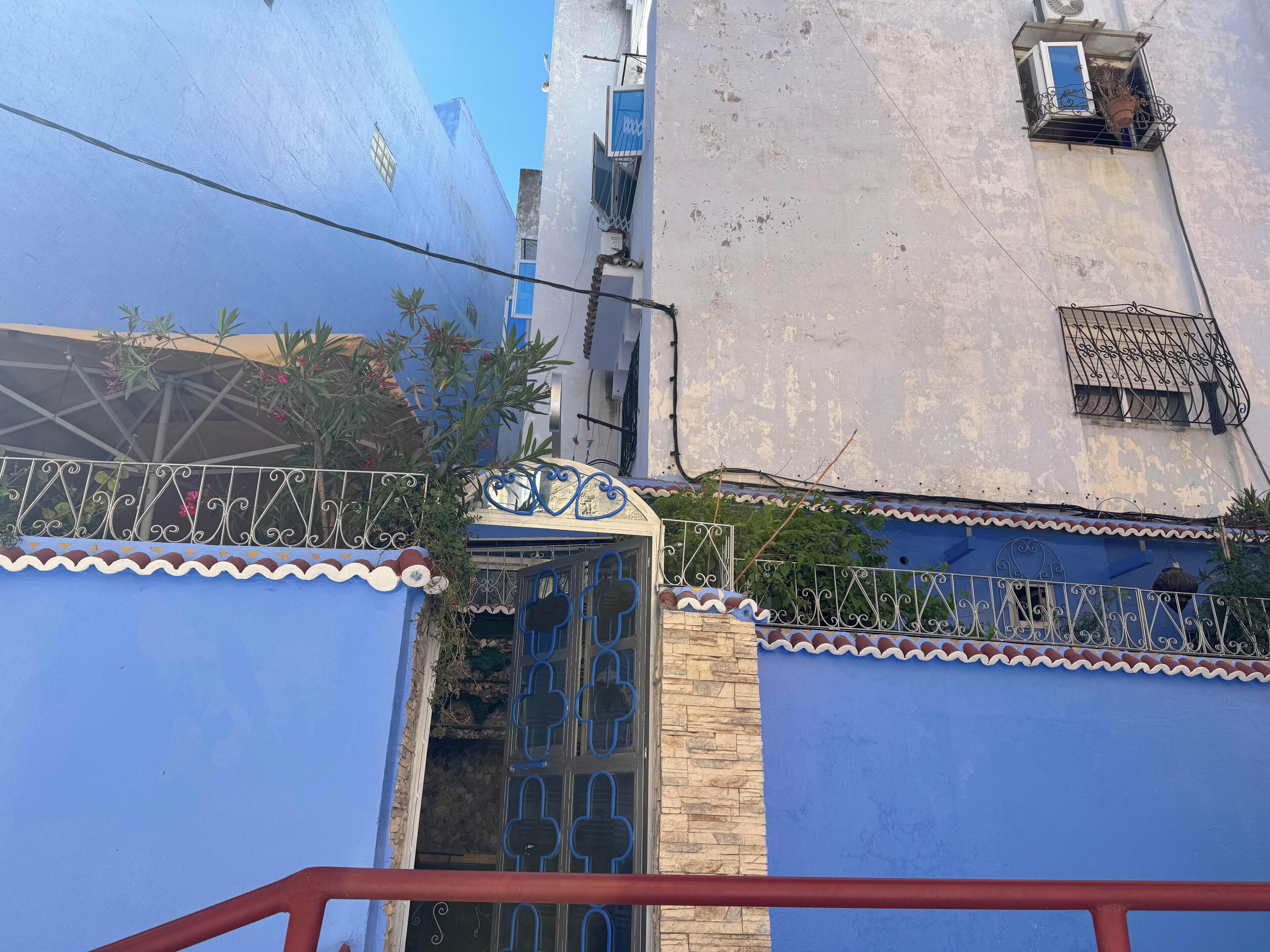 Um edifício azul com entrada protegida por portão, parede de pedra e grade metálica com detalhes decorativos.