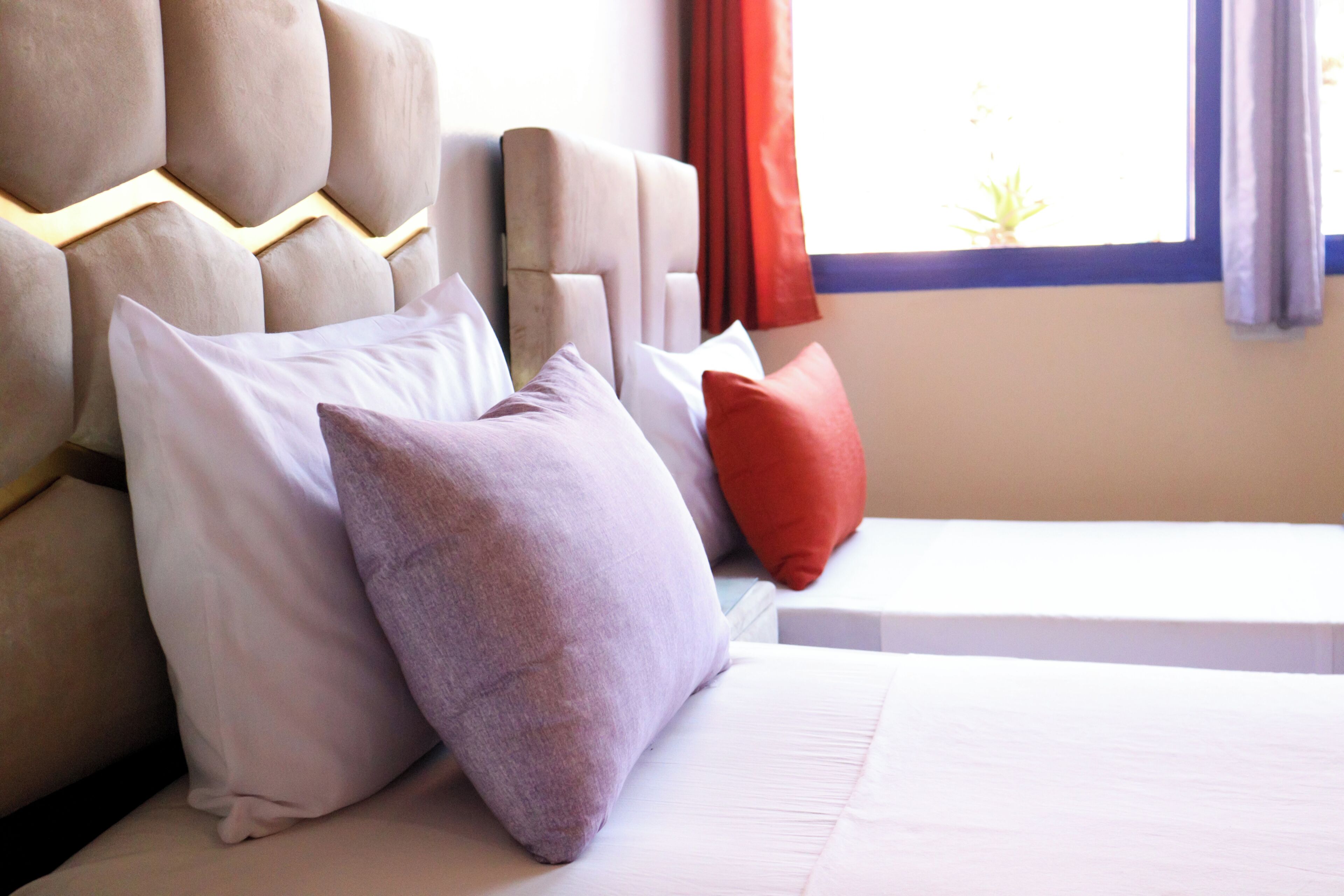 Quarto com cama, almofadas e janela com cortinas.