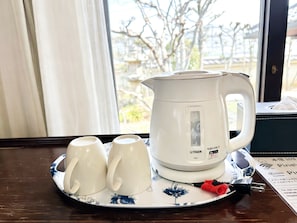Uma chaleira elétrica branca com visor digital, duas xícaras brancas com estampas florais azuis e um prato com um desenho floral.