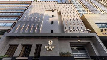 Um hotel moderno com uma placa grande 'BROWN-DOT HOTEL', entrada de garagem e fachada com padrão geométrico.