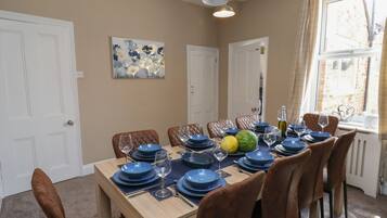 Uma sala de jantar com uma mesa de madeira posta para oito pessoas, cadeiras estofadas marrons e um quadro na parede.