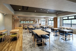 Um espaço amplo e interno com diversos arranjos de assentos, incluindo mesas e cadeiras, e uma cozinha ao fundo.