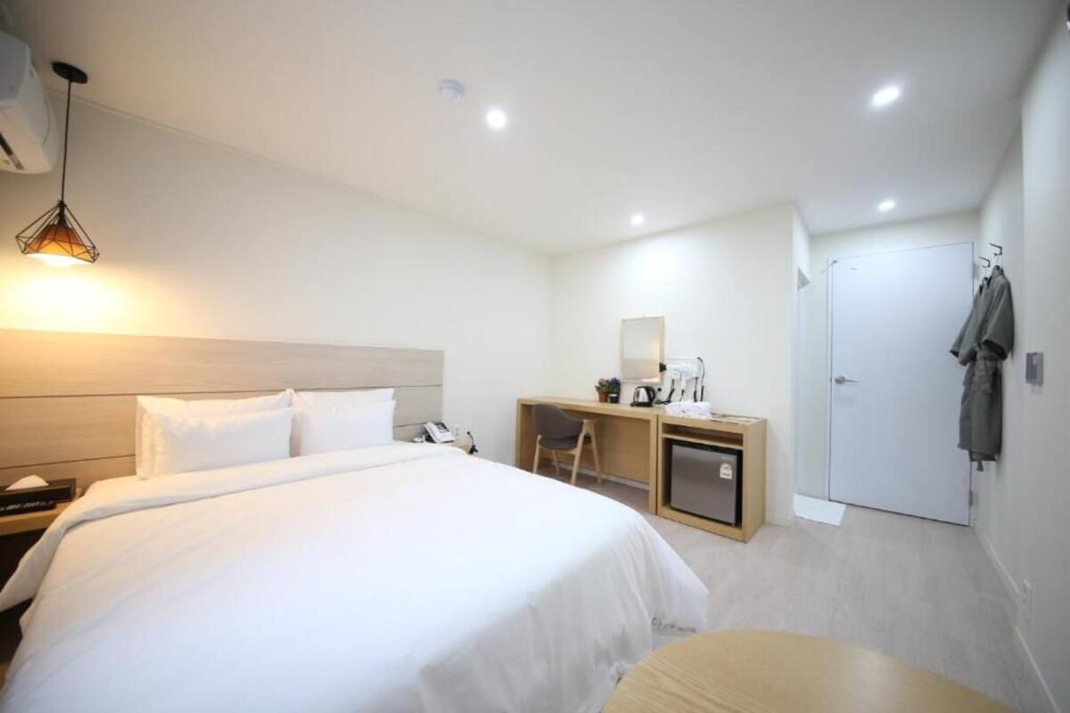 Quarto de hotel com cama, escrivaninha, cadeira e um pequeno frigorífico.