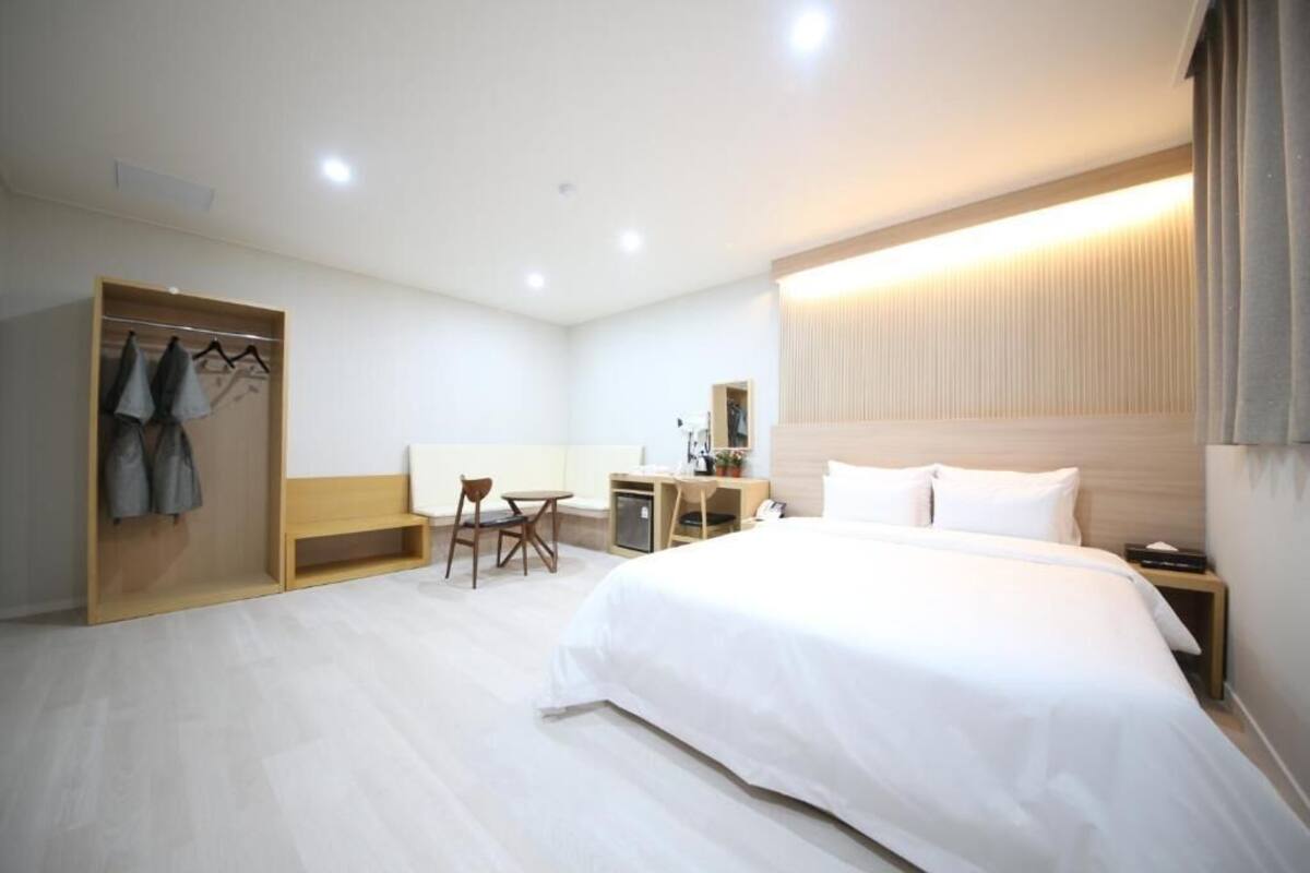 Quarto de hotel com uma cama grande, uma escrivaninha, uma cadeira, um guarda-roupa e uma mesinha de cabeceira.