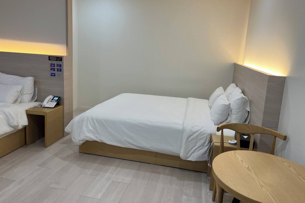 Quarto de hotel com cama, mesa de cabeceira e uma pequena cadeira de madeira.