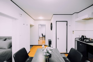 Quarto compacto com mesa de jantar, cadeiras, pequena cozinha e um sofá.
