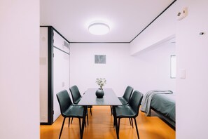 Quarto moderno com mesa de jantar, cadeiras, um vaso com flores, uma cama e uma janela.