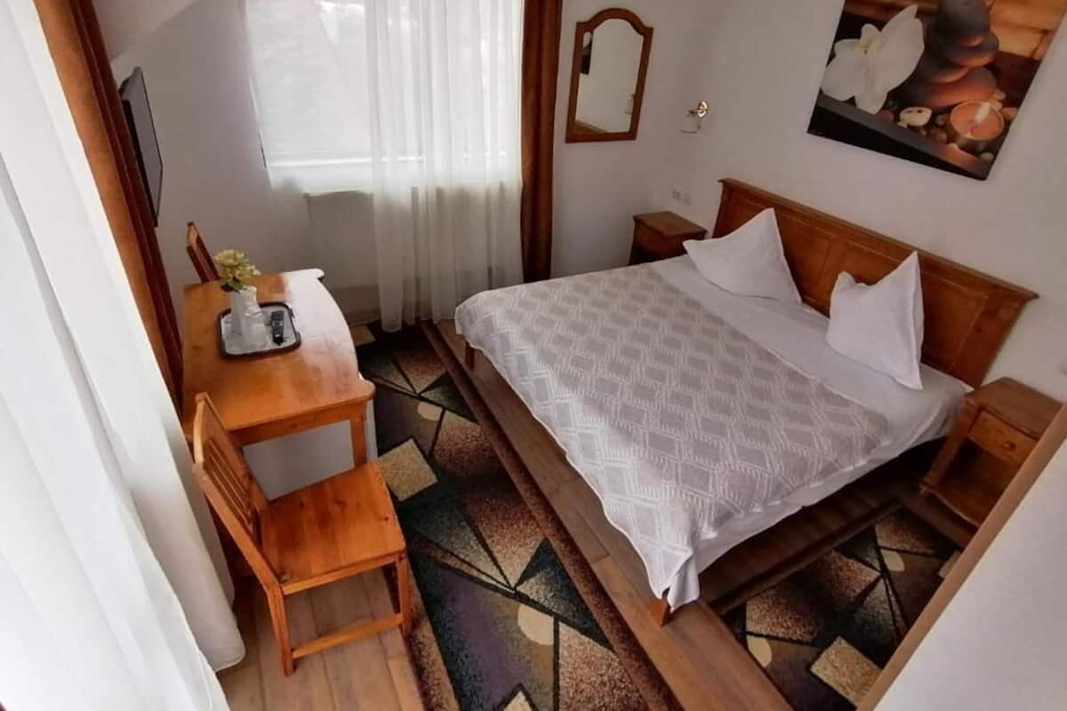 Quarto com cama, escrivaninha de madeira, cadeira, mesa de cabeceira, espelho e um quadro na parede.