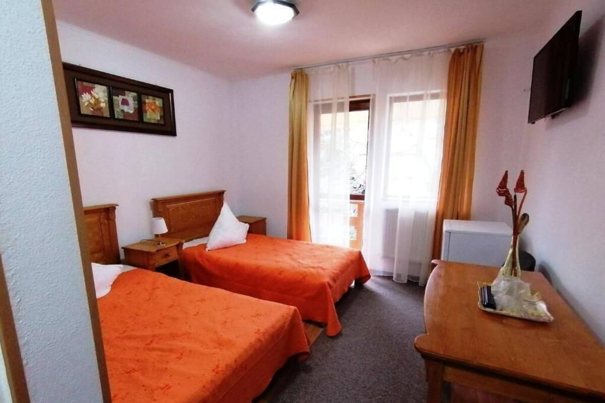 Quarto de hotel com duas camas, uma escrivaninha, televisão e janela com cortinas.
