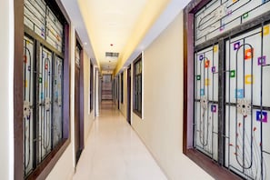 Um corredor de hotel comprido e estreito, com piso de azulejos, portões de metal com desenhos coloridos e um batente de porta de madeira.