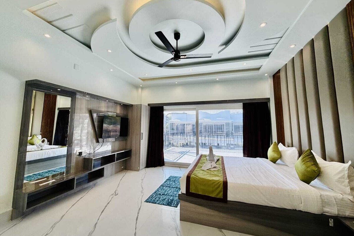 Quarto de hotel moderno com cama, TV, ventoinha no teto e uma janela grande com vista.