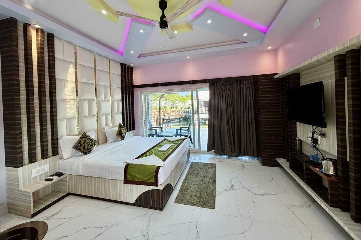Quarto de hotel moderno com uma cama grande, televisão e varanda com mobiliário para área externa.