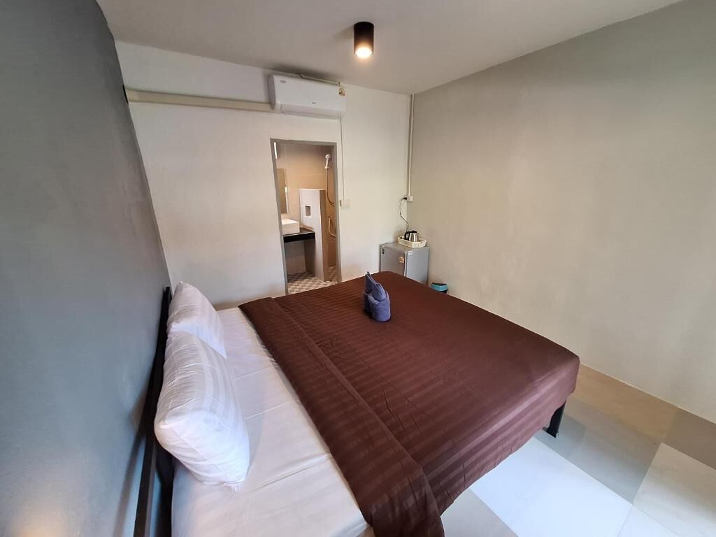 Quarto com cama, mesa de cabeceira, ar condicionado fixado na parede e porta que dá para um banheiro.
