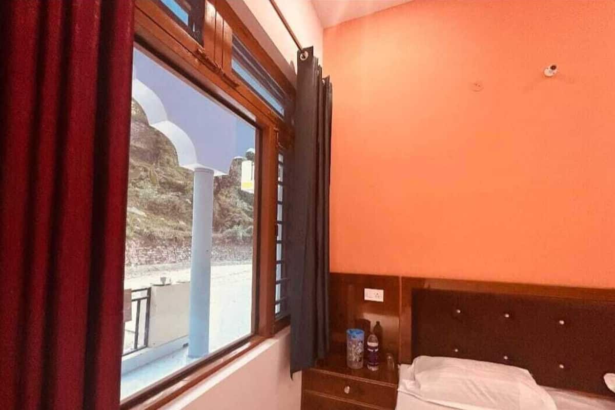 Quarto de hotel com cama, mesa de cabeceira, janela com cortinas e vista para um edifício.