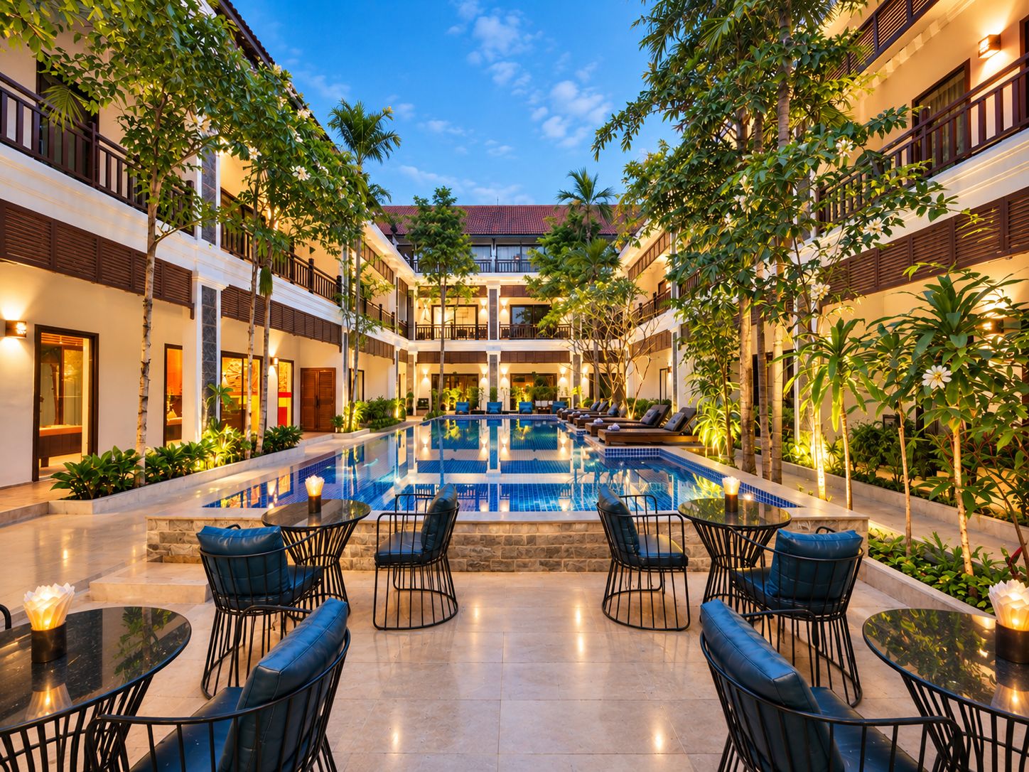 Pátio de hotel com piscina central, espreguiçadeiras e mesas.
