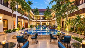Pátio de hotel com piscina central, espreguiçadeiras e mesas.