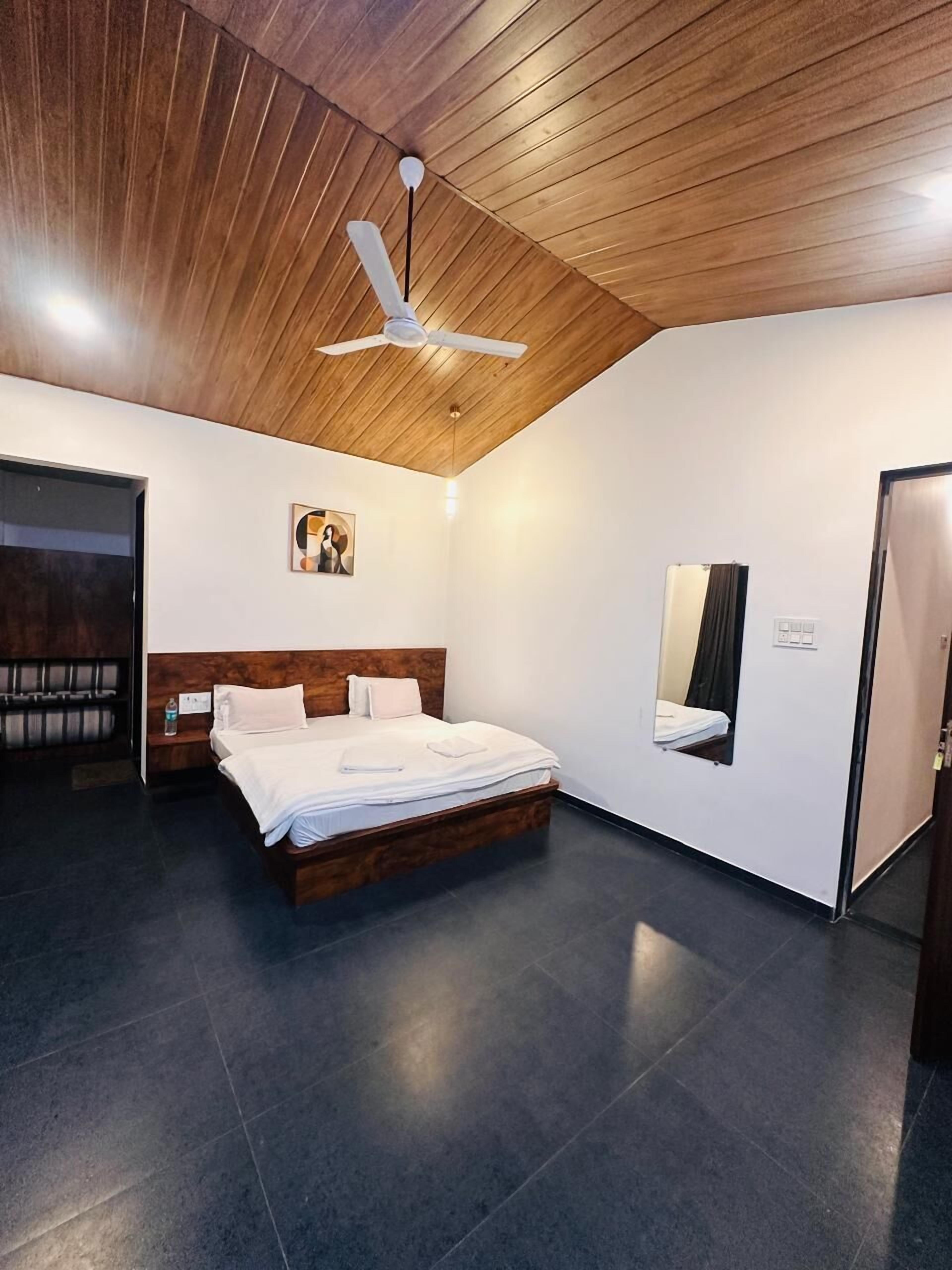 Quarto moderno com teto de madeira, cama com roupa de cama branca, mesa de cabeceira com garrafa de água e espelho na parede.