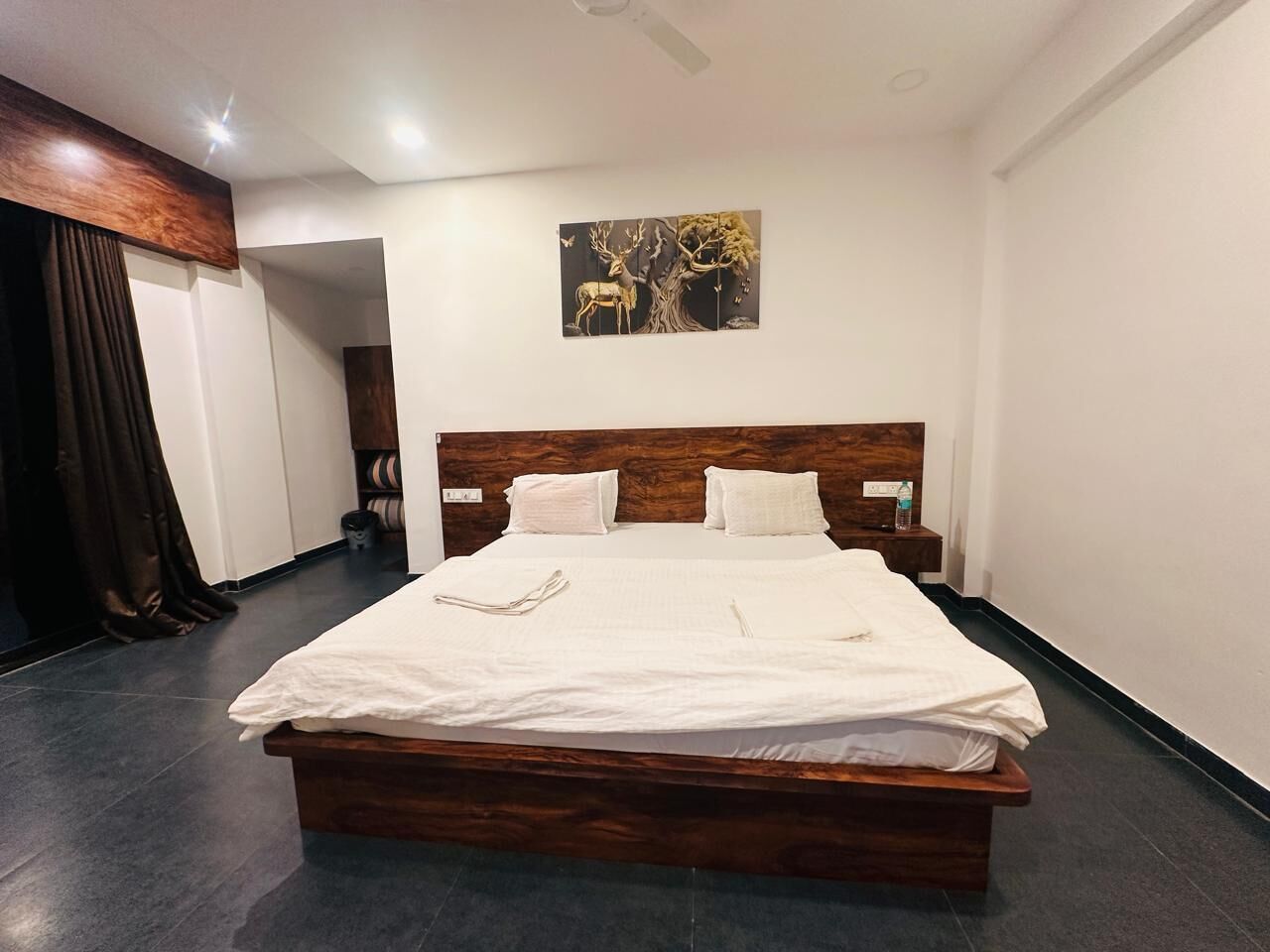 Cama bem arrumada com cabeceira de madeira, uma obra de arte na parede e piso escuro.