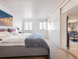 Quarto com cama, duas janelas, um quadro e vista para a cozinha.