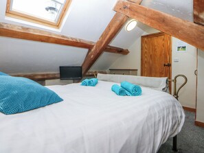 Quarto com cama, toalhas dobradas, televisão e estrutura de teto em madeira.