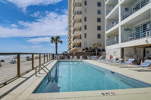 Piscina com espreguiçadeiras, um deck de madeira e vista para a praia.