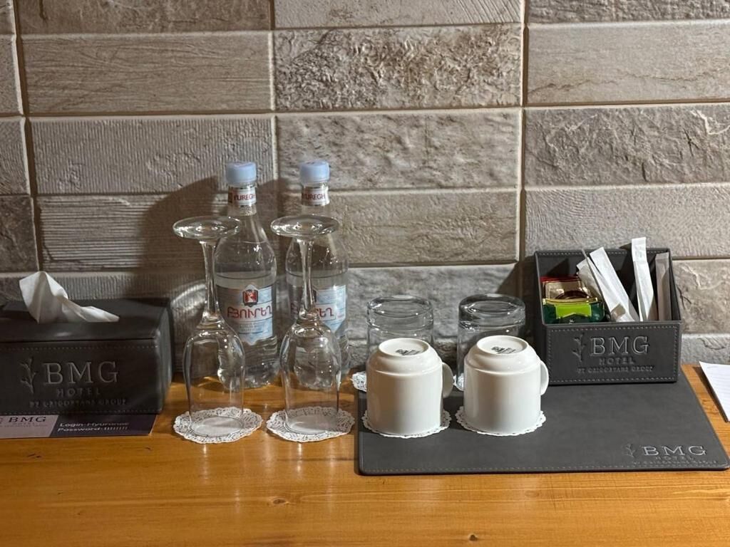 Quarto de hotel com painel de azulejos, minibar e bandeja com copos e garrafas.
