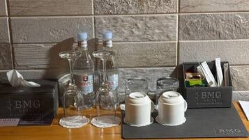 Quarto de hotel com painel de azulejos, minibar e bandeja com copos e garrafas.