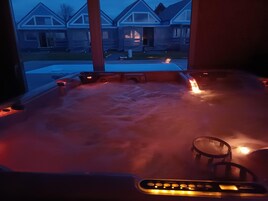 Uma banheira de hidromassagem com controle remoto, vapor subindo e vista para casas pela janela.
