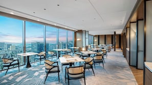 Um lobby de hotel moderno com tetos altos, grandes janelas e vista para a cidade.
