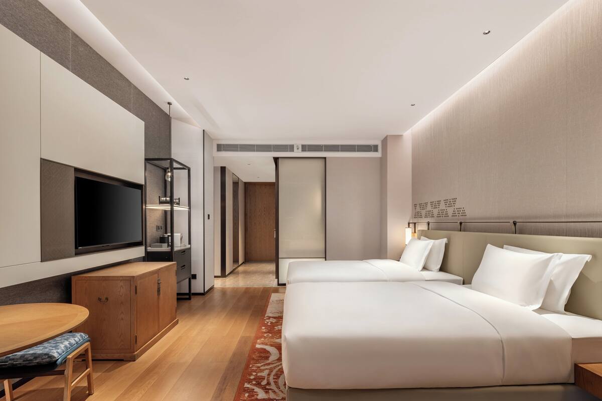 Quarto de hotel moderno com uma cama grande, televisão, armário de madeira e escrivaninha com cadeira.