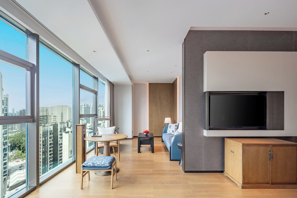 Uma sala de estar moderna com uma TV grande, uma área de refeições e vista para a cidade através de amplas janelas.