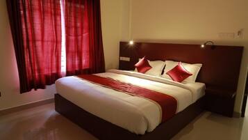 Quarto com cama, cortinas, mesa de cabeceira e luminária fixada na parede.