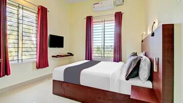 Quarto de hotel com cama, televisão, ar condicionado e janela com cortinas.
