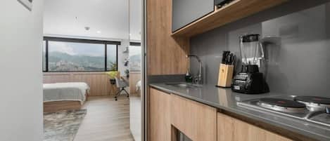 Cozinha moderna com vista, armários de madeira, micro-ondas preto, cafeteira e liquidificador.