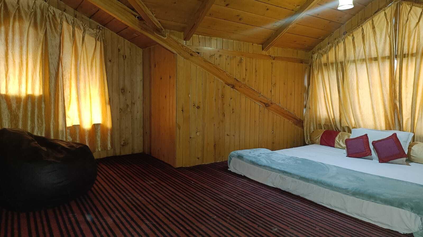 Quarto de madeira com cama, cortinas e um puff.