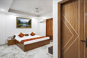 Quarto de hotel com cama, mesa de cabeceira, pintura, ventoinha de teto e porta de madeira.