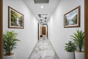 Um corredor com piso de mármore, quadros de paisagens e plantas em vasos.
