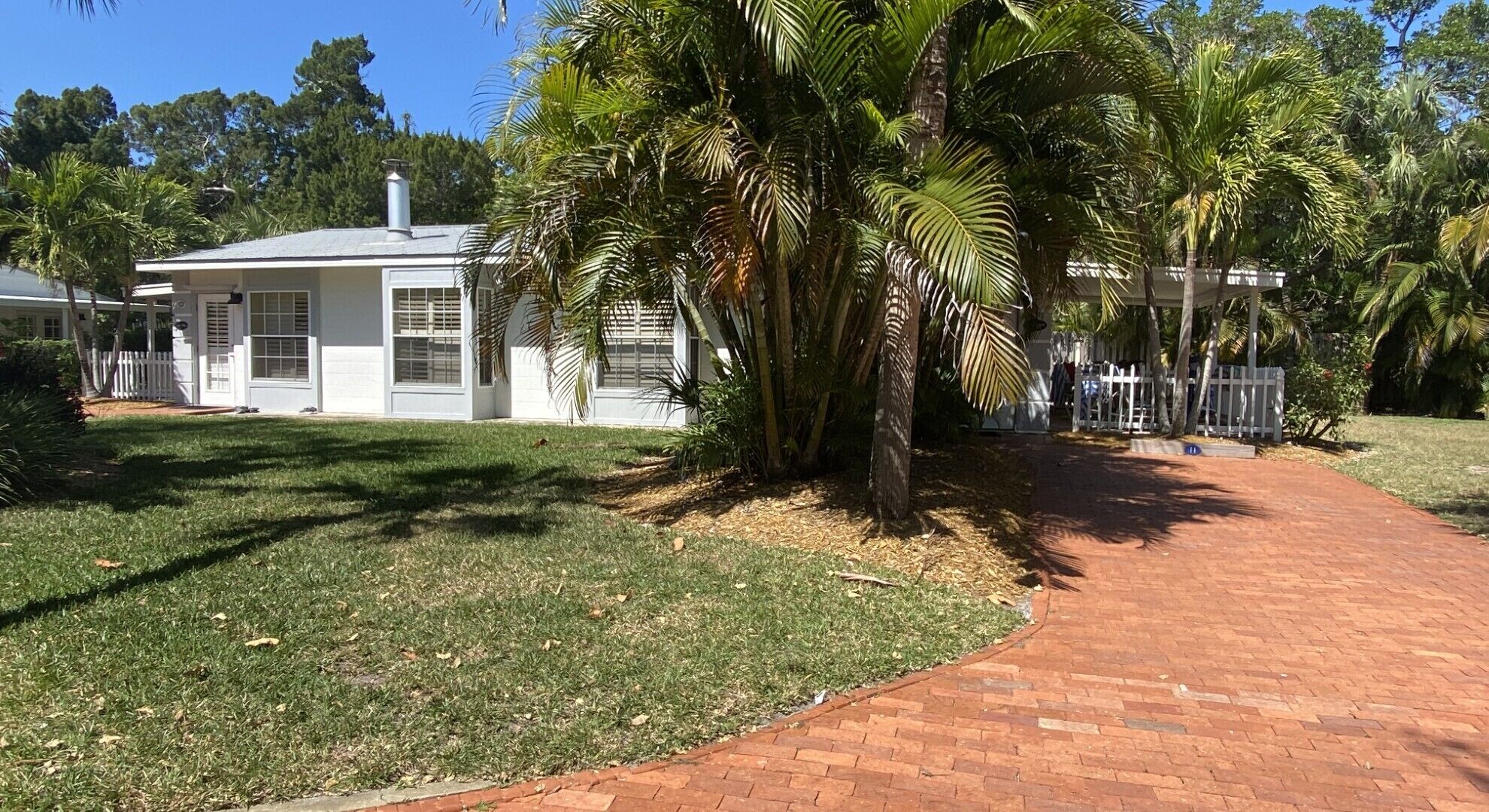 Uma casa com um caminho de tijolos que leva a um edifício branco, com janelas e varanda coberta.