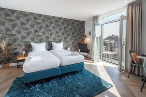 Quarto de hotel moderno com uma cama grande, varanda e vista, e parede com padrão de pedra.