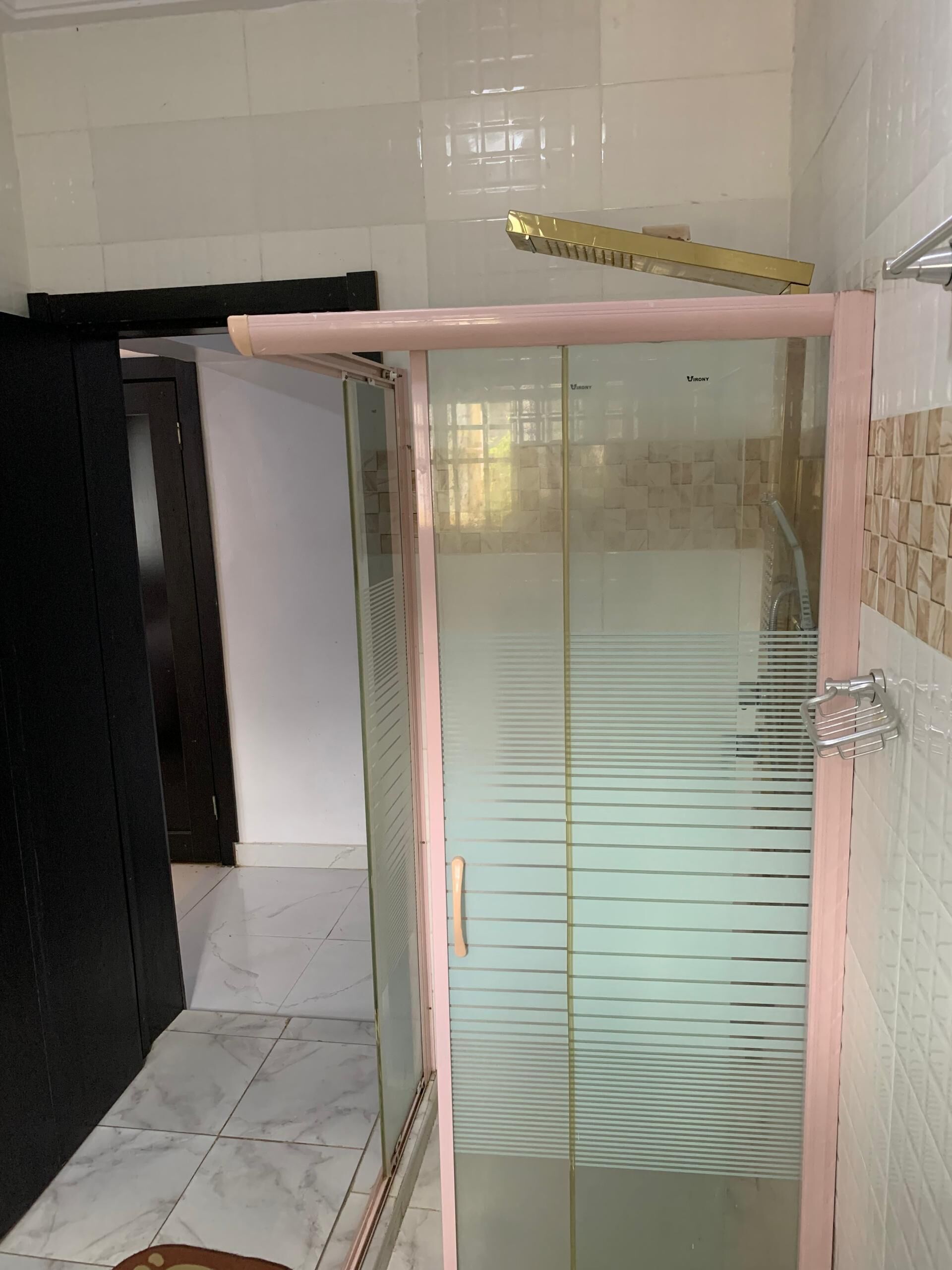 Um chuveiro com divisória de vidro e estrutura rosa, um porta-toalhas e um chão revestido com azulejos.