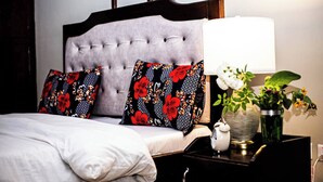 Uma cama bem arrumada com almofadas florais, um abajur e um vaso com flores.