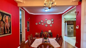 Uma sala de jantar com parede vermelha, um lustre e uma geladeira ao fundo.