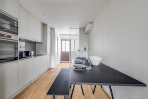 Cozinha moderna com armários brancos, forno Bosch e área de refeições com mesa e cadeiras pretas.