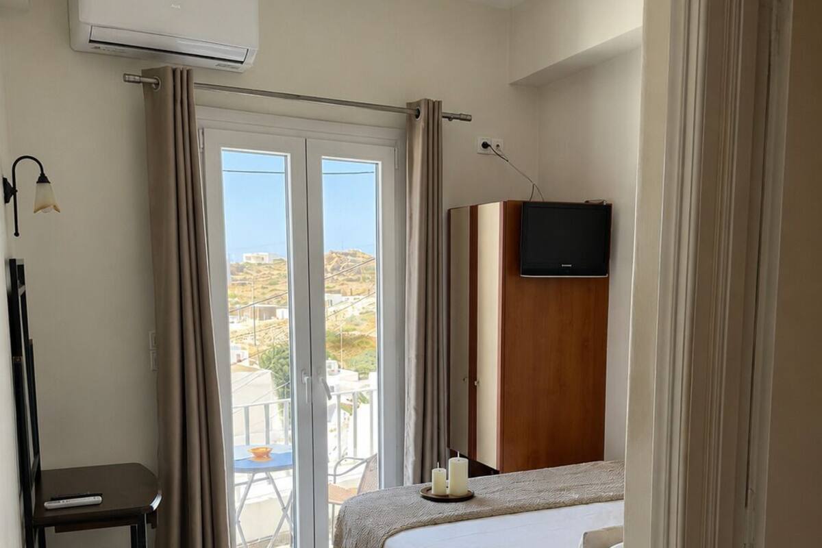 Quarto de hotel com cama, escrivaninha, cadeira, ar condicionado, televisão e vista para o exterior.